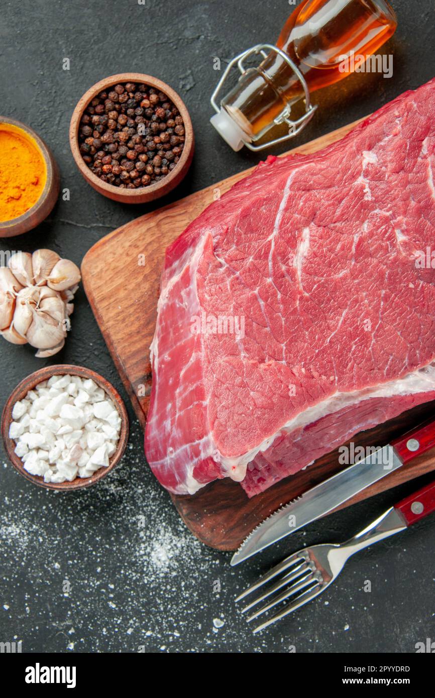 top view raw meat slice with tomatoes and seasonings on a dark ...