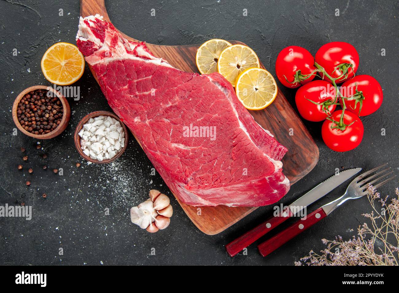 top view raw meat slice with tomatoes and seasonings on dark gray ...