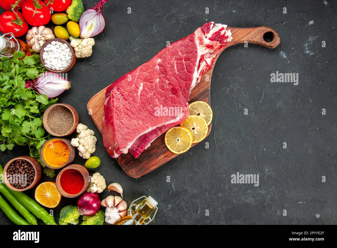 top view raw meat slice with vegetables greens and seasonings on dark ...