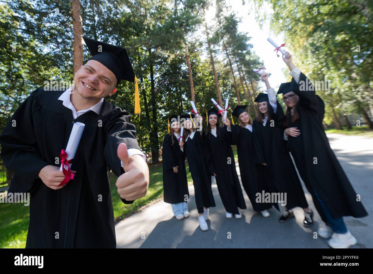 Happy young caucasian male graduate showing thumbs up. A group of ...