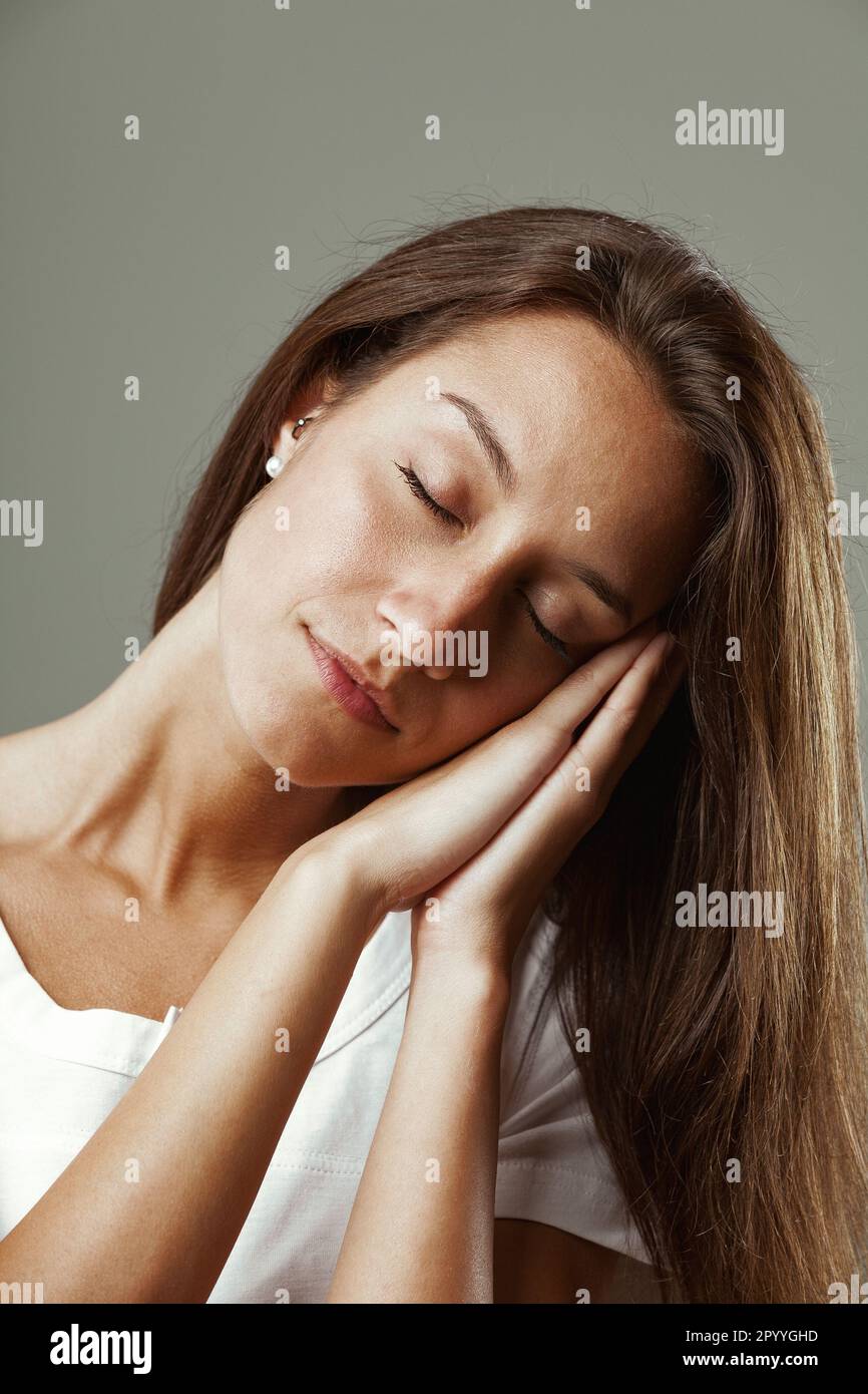 Beautiful young woman with long hair mimics sleeping gesture, hands ...