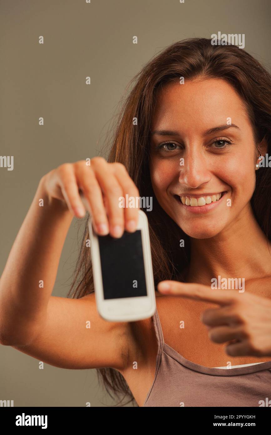 Girl looks at us, points to empty COPYSPACE screen of an old cell phone with an enthusiastically ...