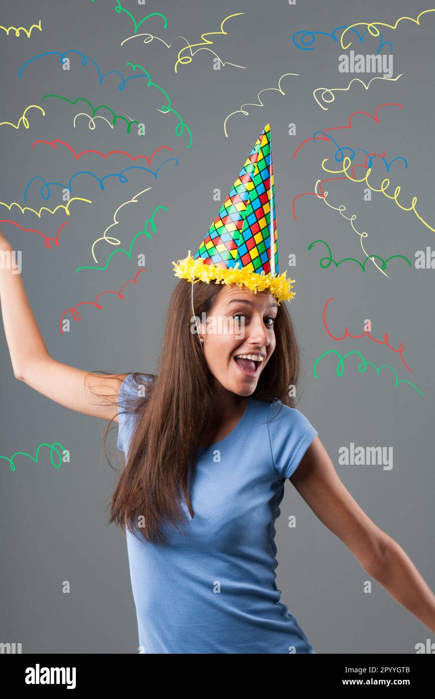 Girl in pointed hat, harlequin colors, and party horn enjoys amidst an ...