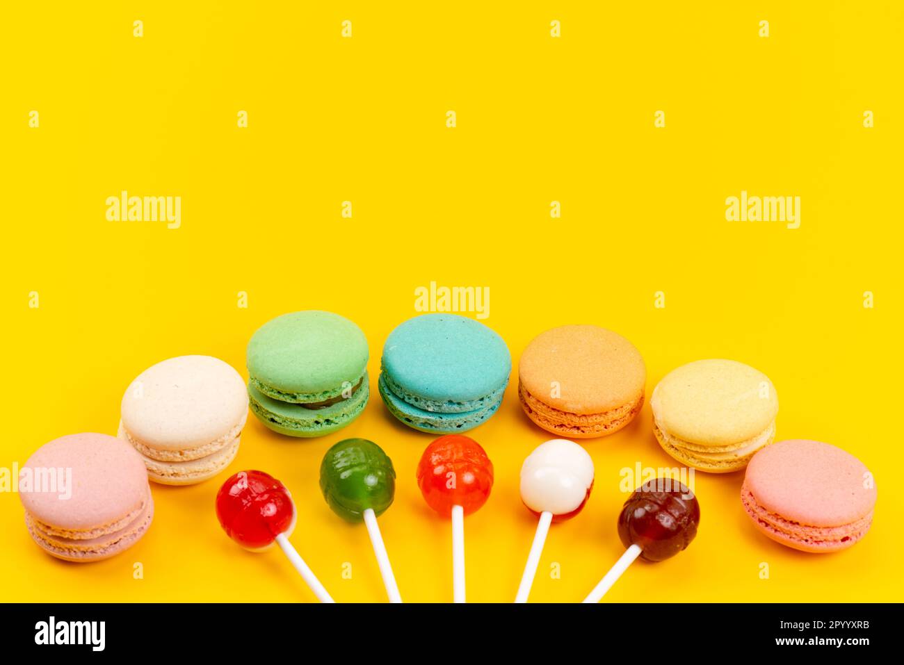 a front view french macarons with lollipops on the yellow desk sugar ...