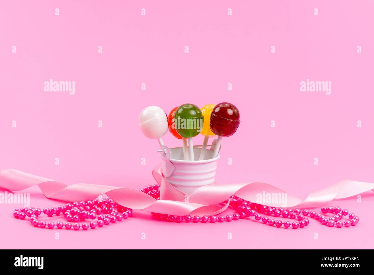 a front view colorful lollipops inside white bucket on the pink desk ...