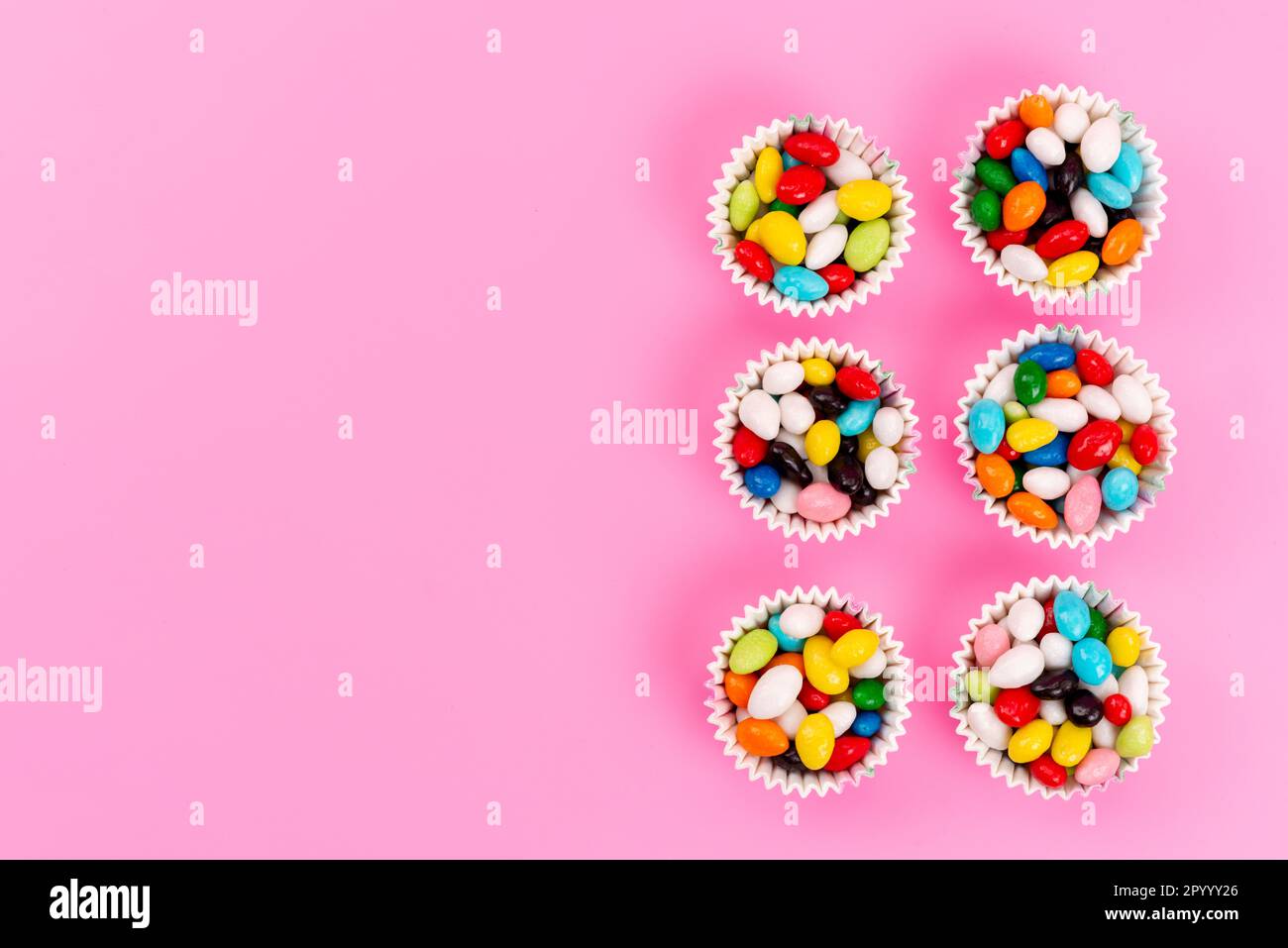 a top view colorful candies inside paper packages on the pink ...