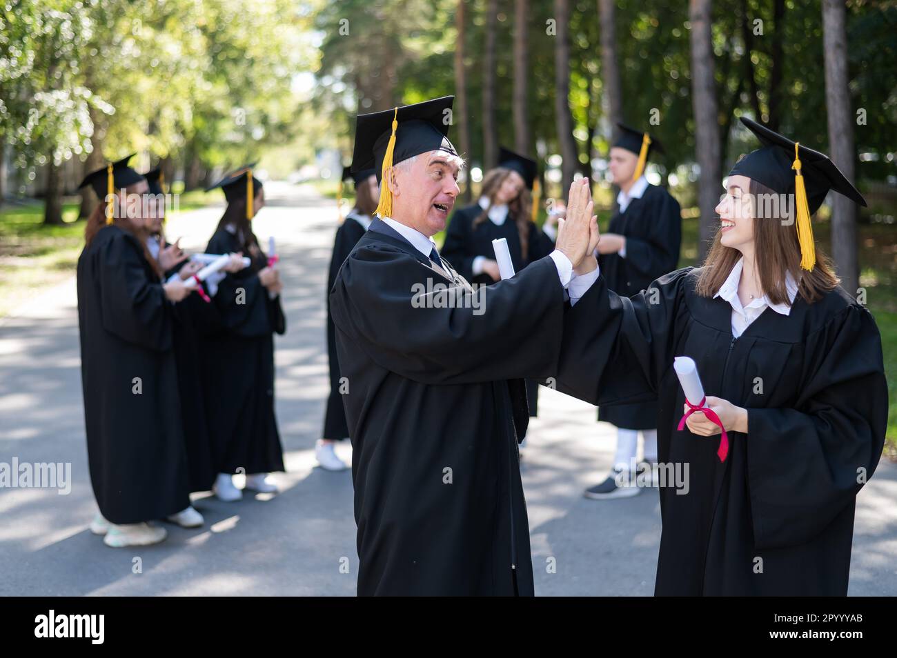A group of graduates in robes outdoors. An elderly man and a young ...
