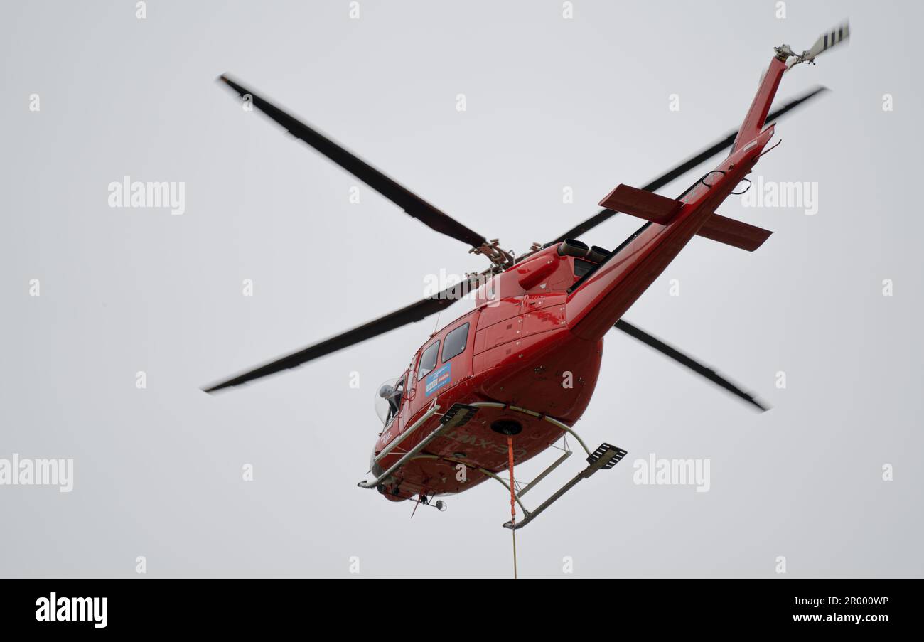 A vibrant red helicopter is seen alighting on a wire rope, with two ...