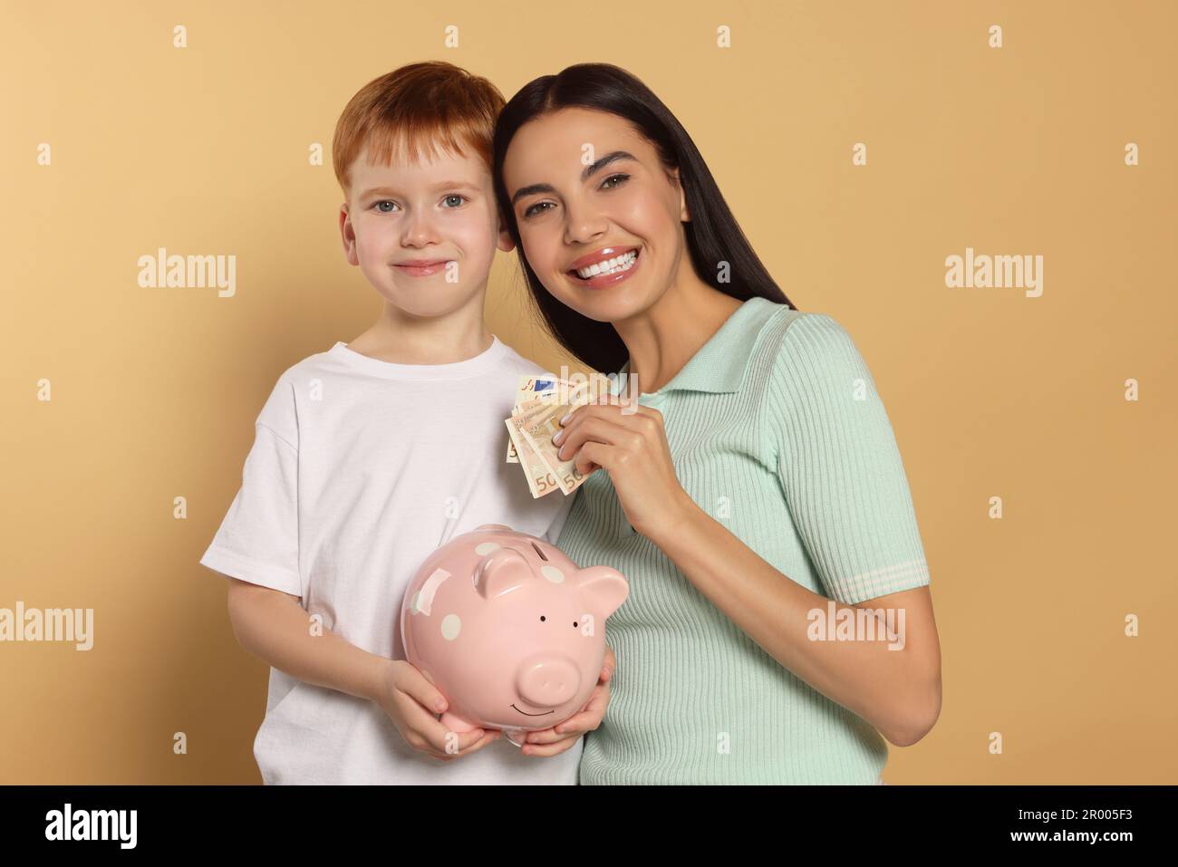 Mother and her son with ceramic piggy bank on beige background Stock ...