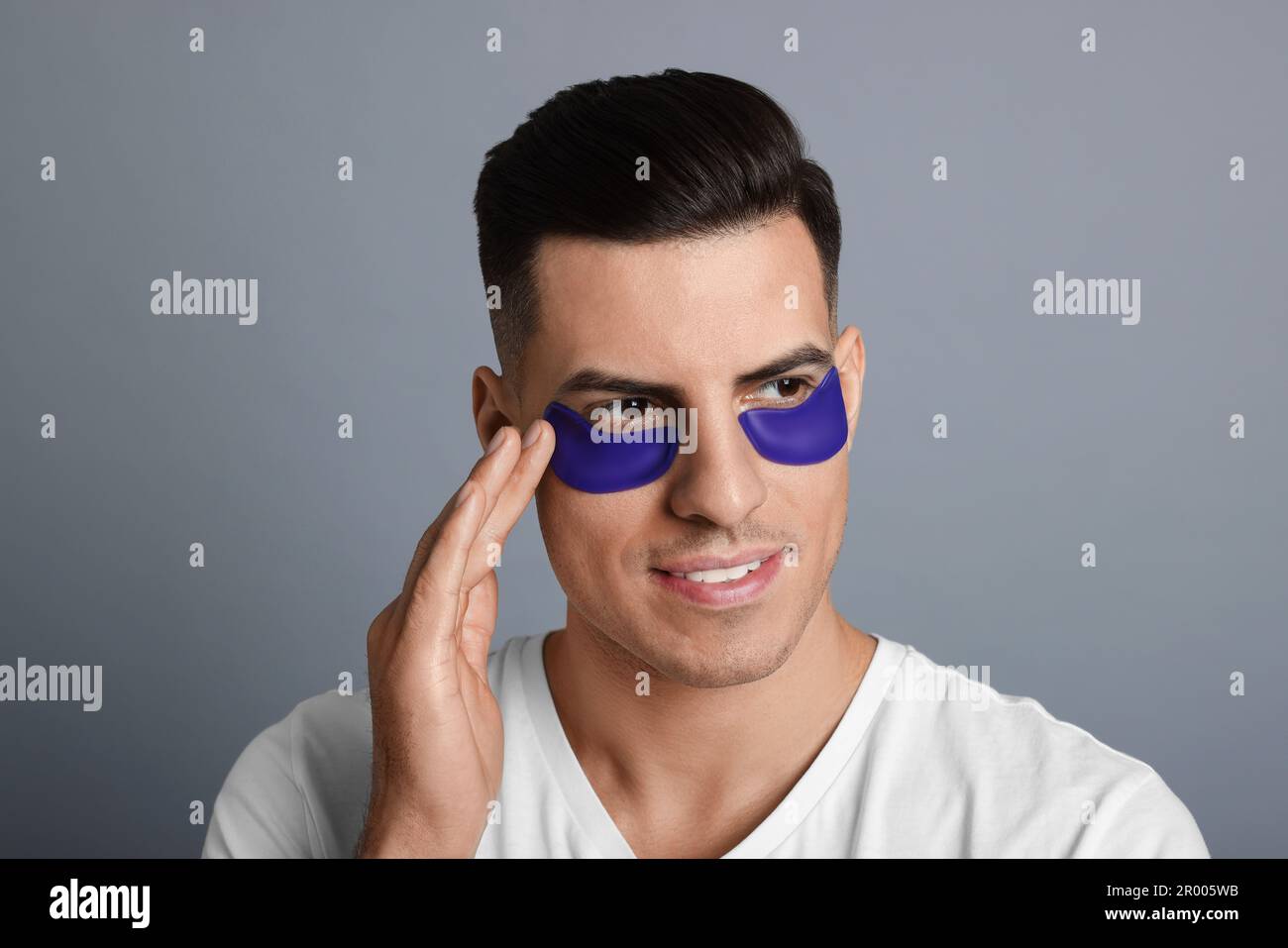 Man applying blue under eye patch on grey background Stock Photo - Alamy
