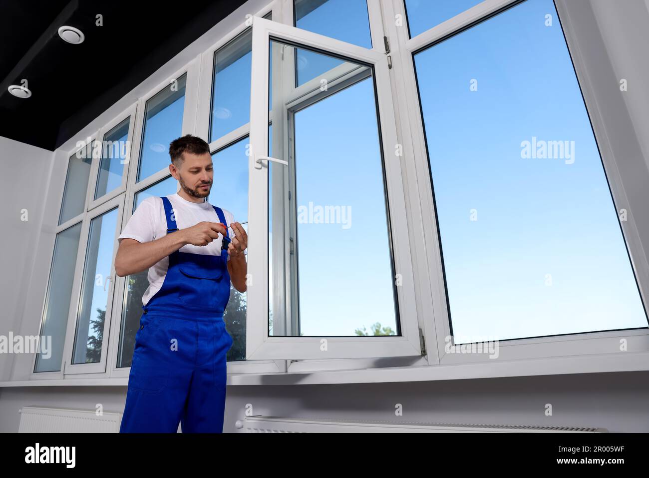 Construction worker adjusting installed window with screwdriver indoors ...