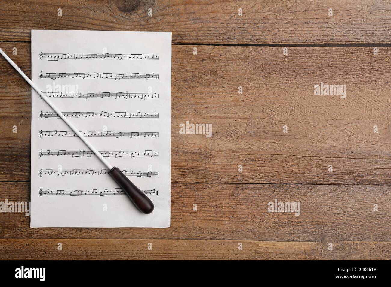 Conductor's baton and sheet music on wooden table, top view. Space for ...