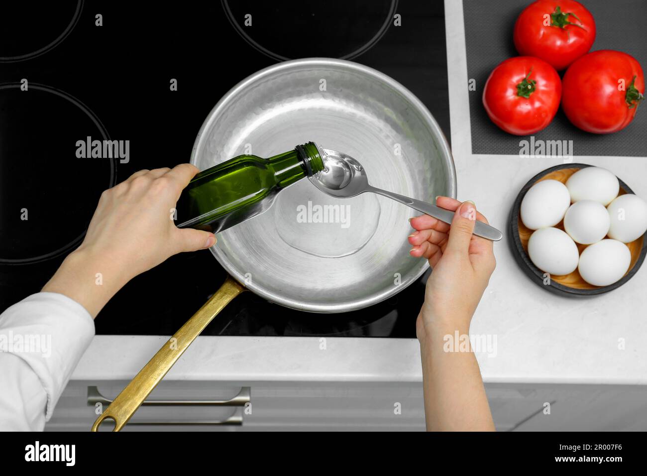 Woman pouring cooking oil from bottle into frying pan in kitchen, top ...