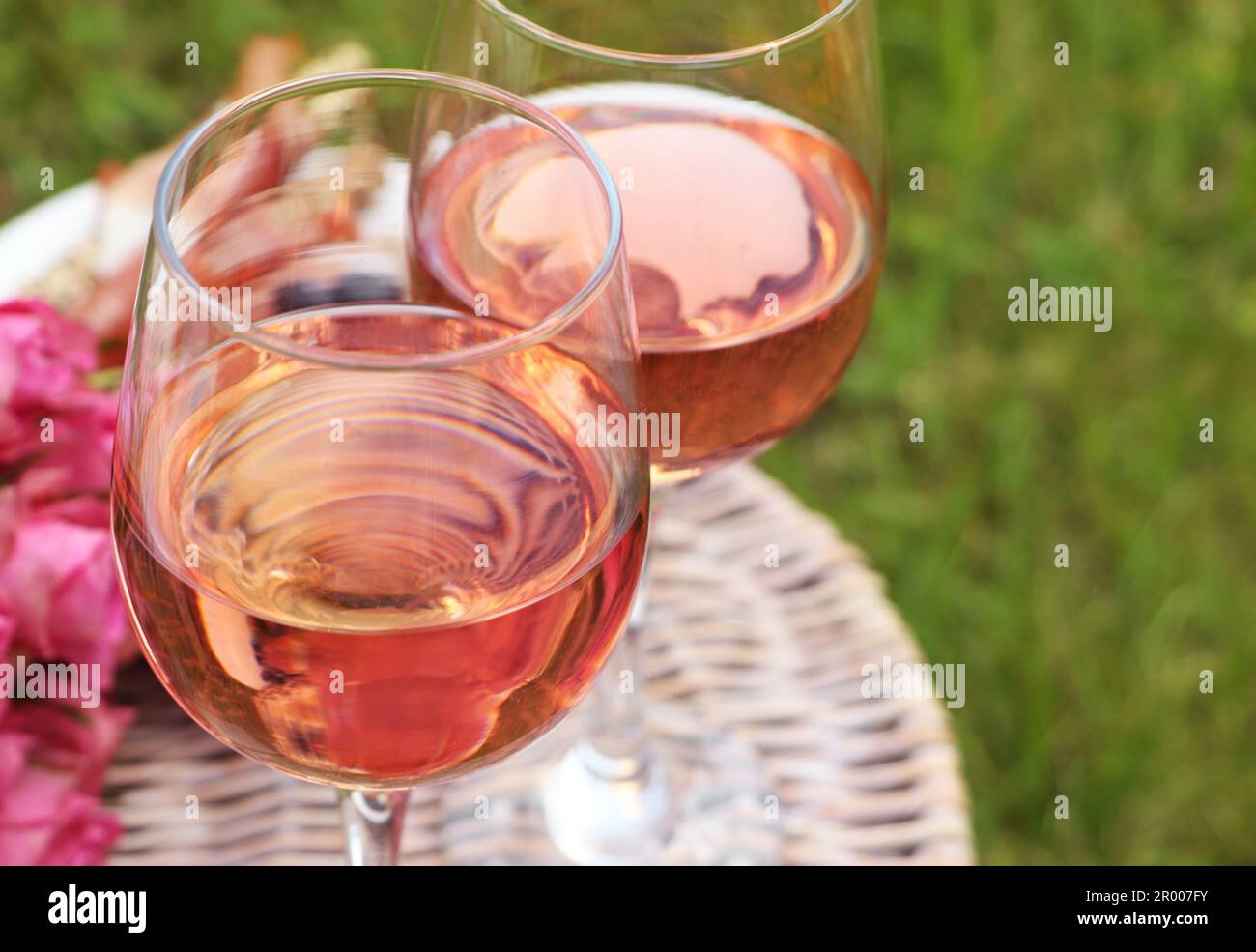 Glasses of delicious rose wine and flowers on picnic basket outdoors ...