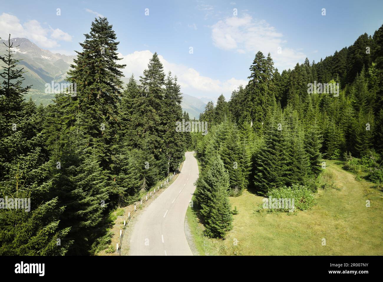 Beautiful road with trees near mountains under light blue cloudy sky ...