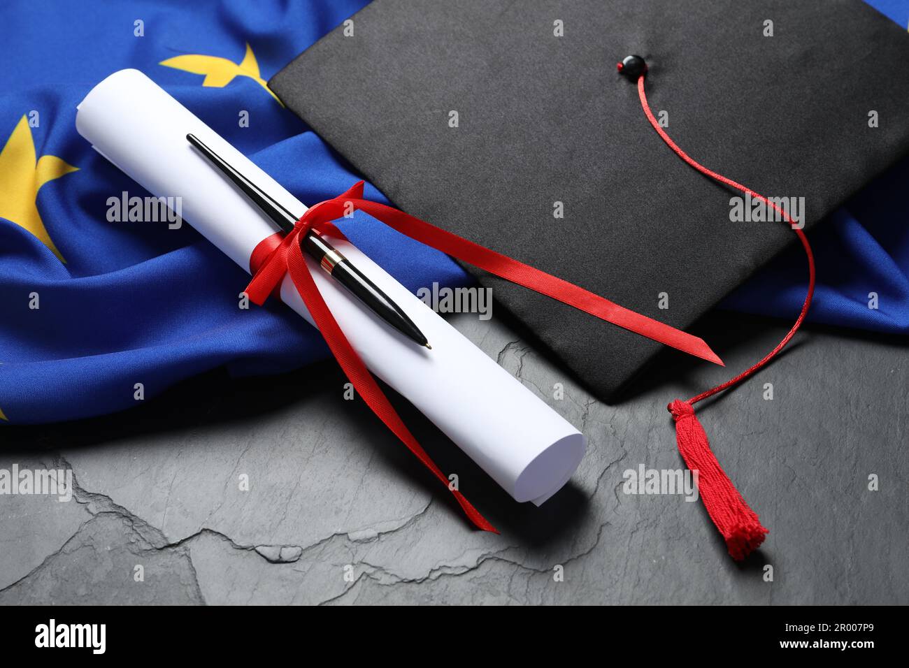 Graduation cap, diploma, pen and flag of European Union on black table ...