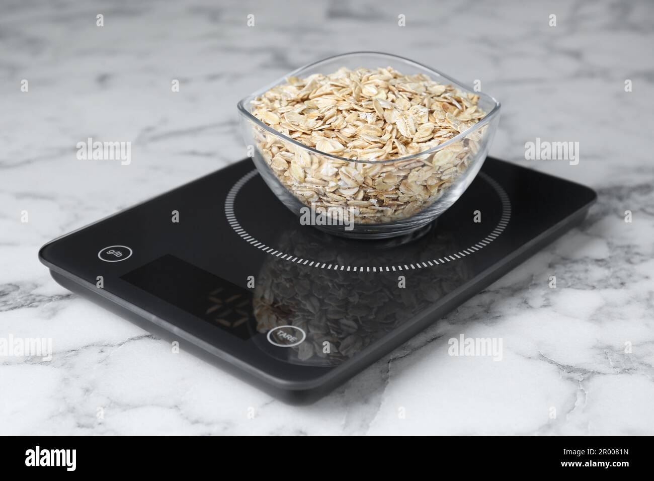 Digital kitchen scale with oat flakes on white marble table Stock Photo ...