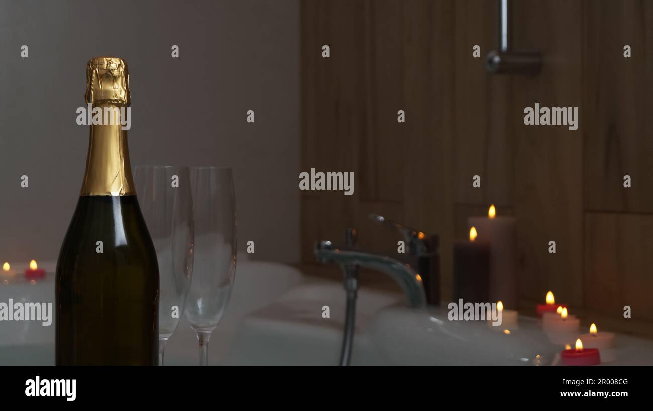 Bottle of champagne, glasses and burning candles near jacuzzi in ...