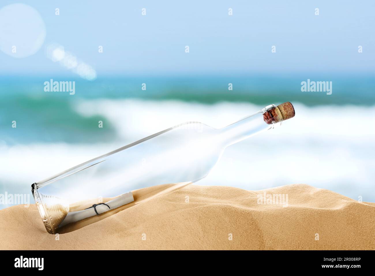 Corked glass bottle with rolled paper note on sandy beach near ocean ...