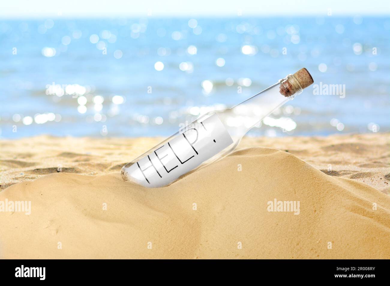 Corked glass bottle with rolled paper note on sandy beach near ocean ...