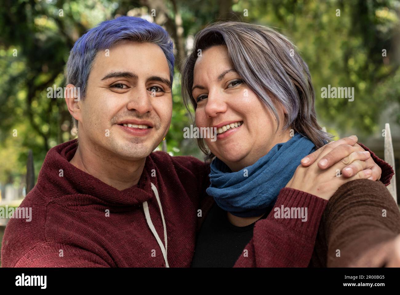 Two smiling friends are hugging and looking at camera. He has blue hair ...