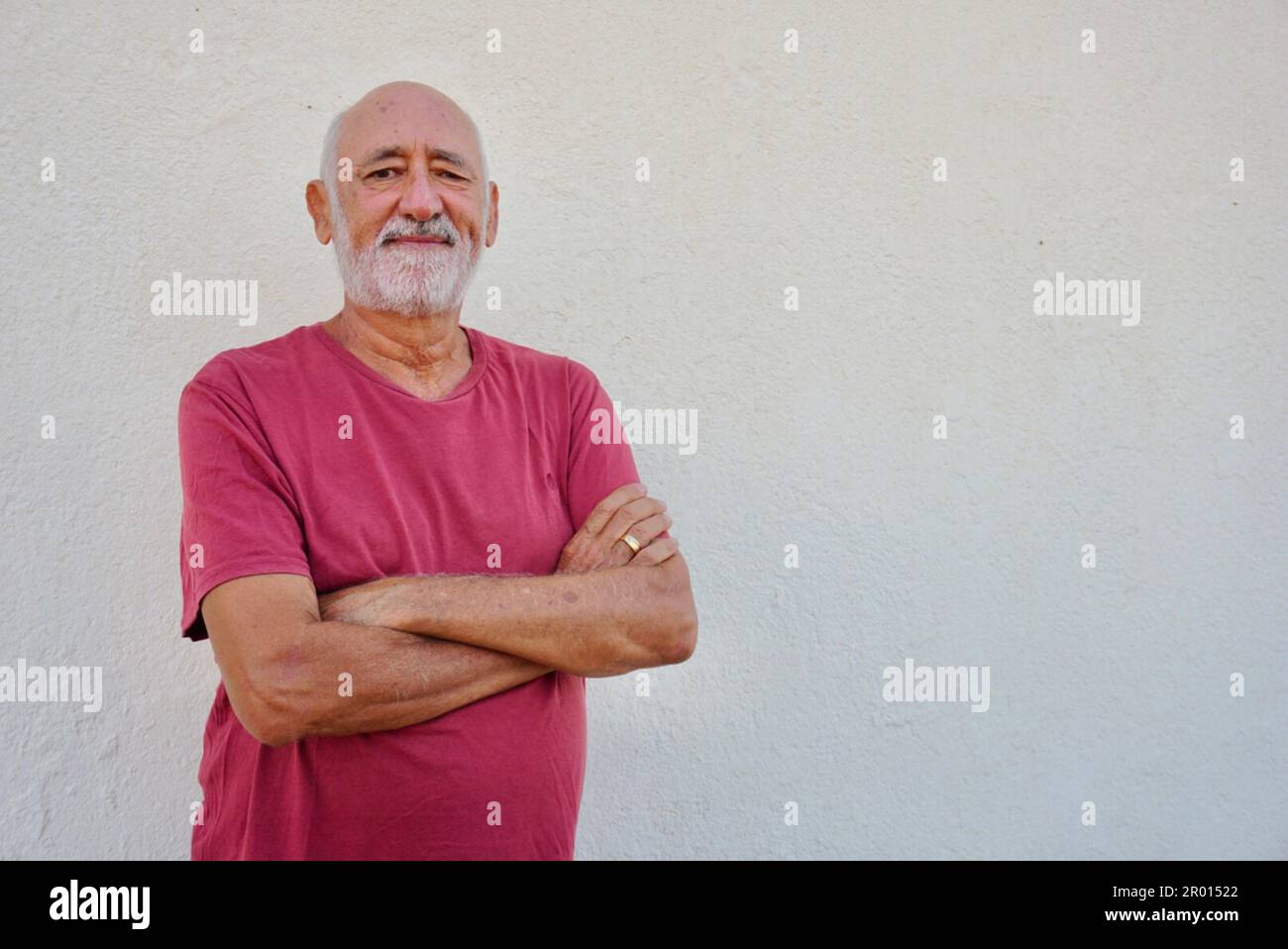 A mature elderly man wearing pink shirt and standing against white wall ...