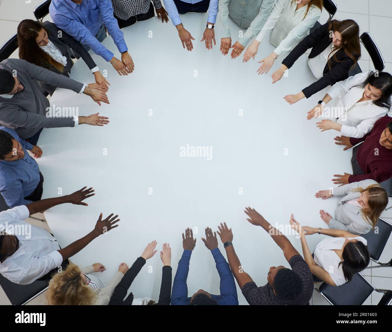 a large group of people sitting at a round table with their arms ...