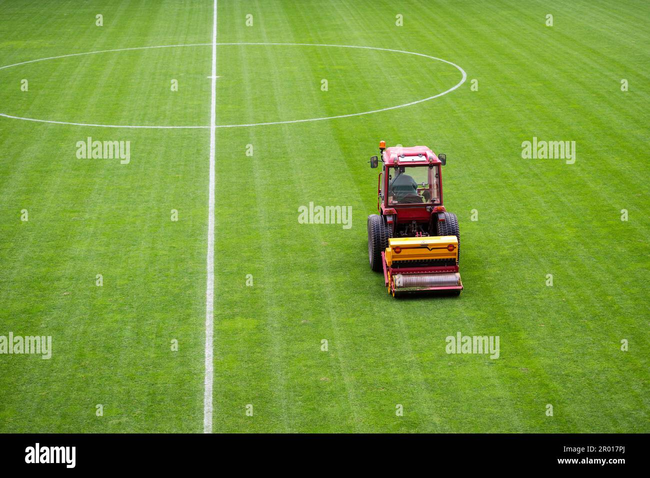 A man in a tractor with a disc seeder drill sowng grass at the football ...