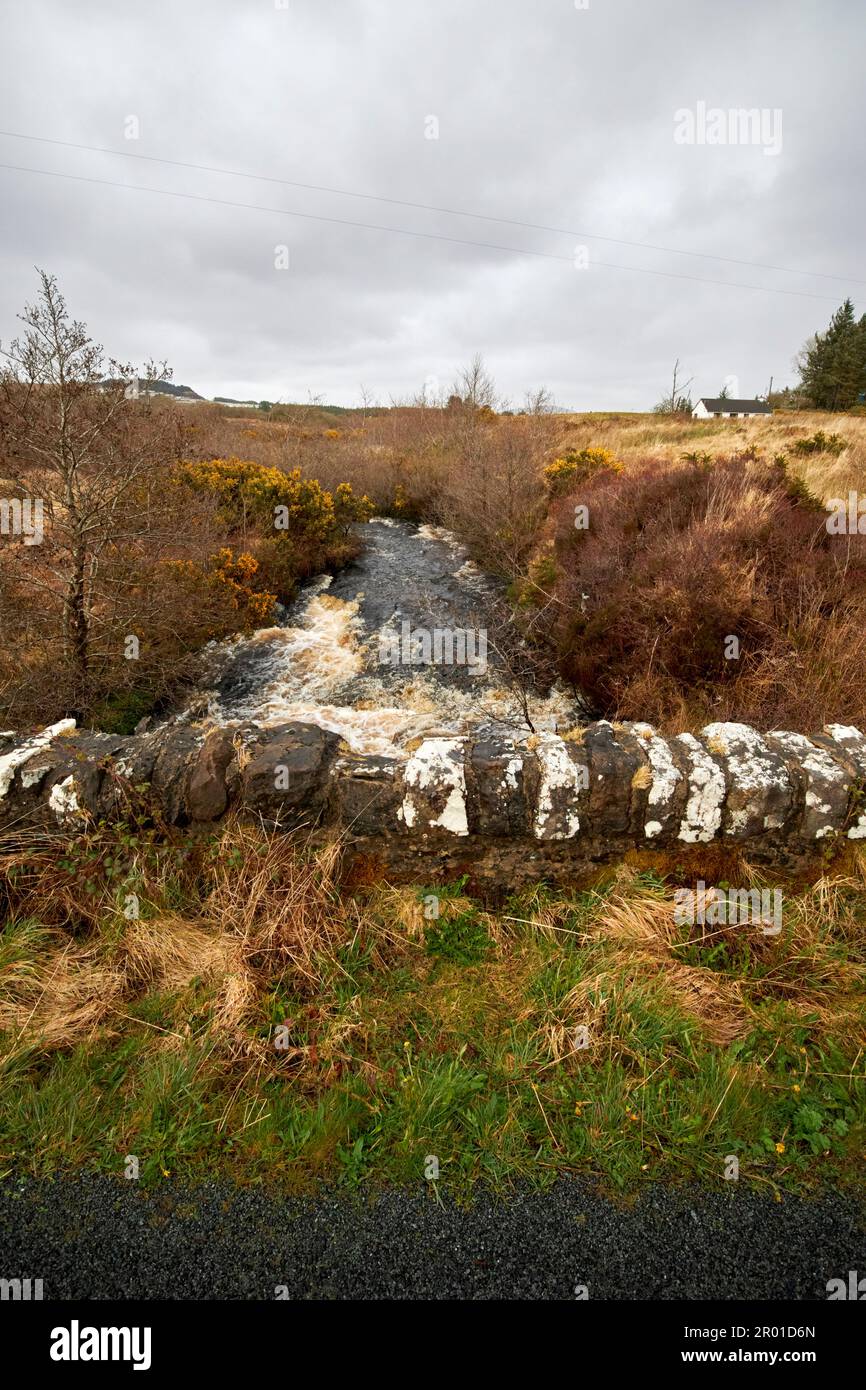 road and old stone bridge over small stream river in flood in remote ...