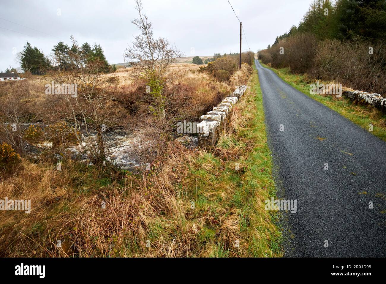 resurfaced rough tarmac road over bridge with fast flowing stream river ...