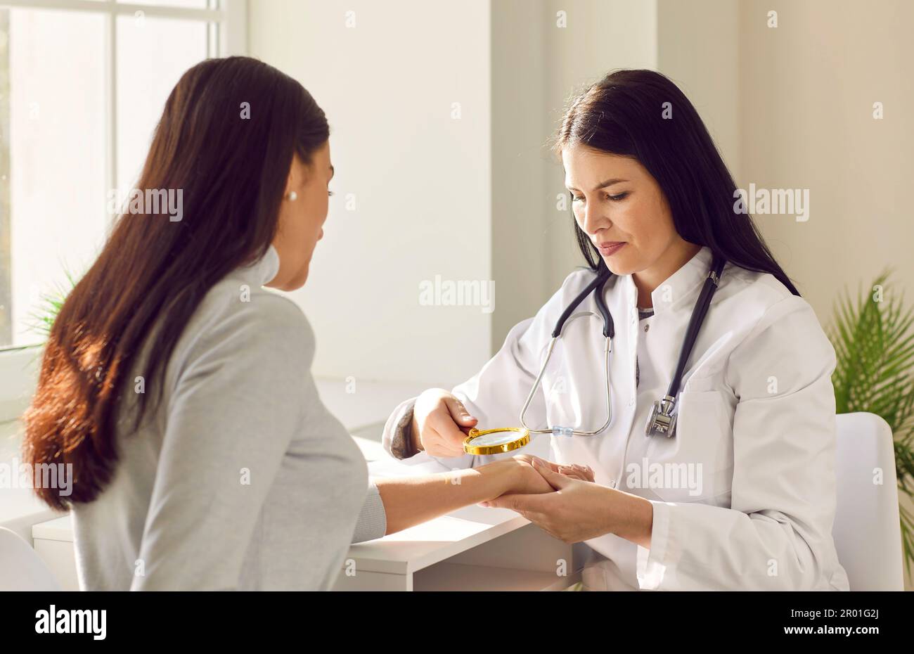 Female doctor examining hand skin of a young woman patient using ...
