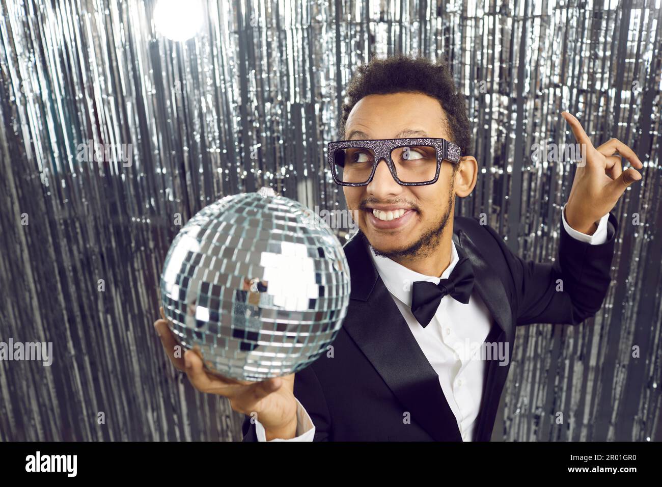 Cheerful young dark-skinned disco man in suit with shiny silver mirror ...