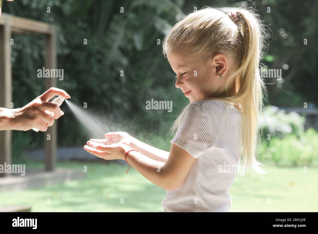 Mother applying hand sanitizer or mosquito repellent spray on her child ...