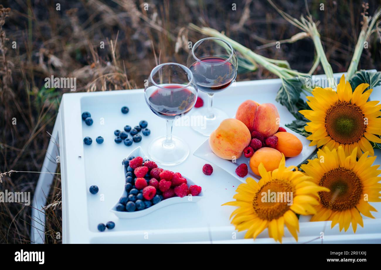Romantic picnic in nature. Two glasses of red wine, berries and fruits ...