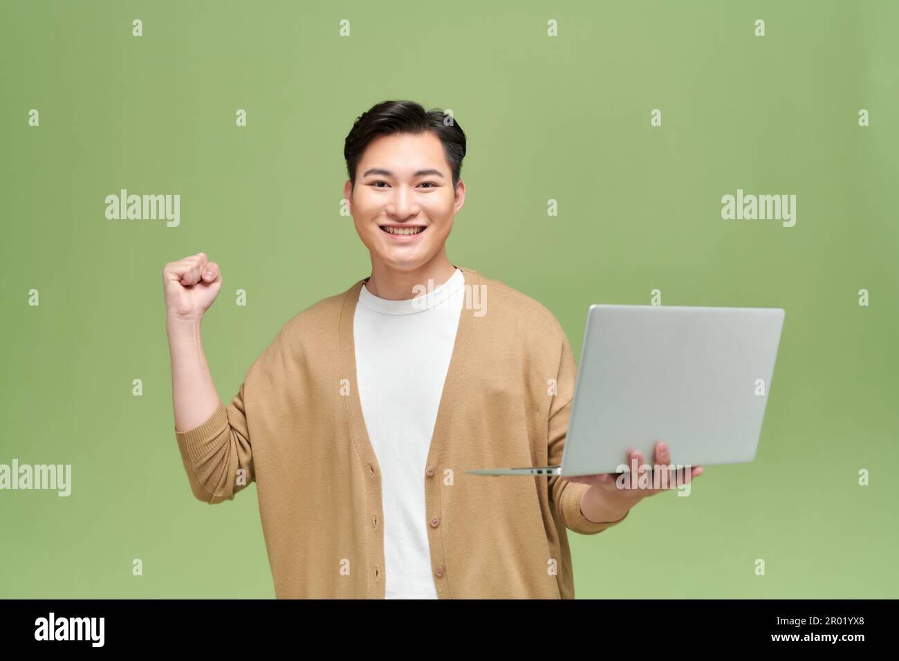 Happy excited Asian man holding laptop and raising his arm up to ...