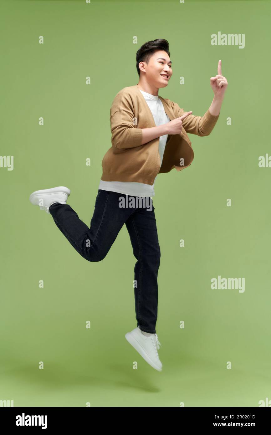Energetic excited young Asian man jumping and pointing hand to empty ...