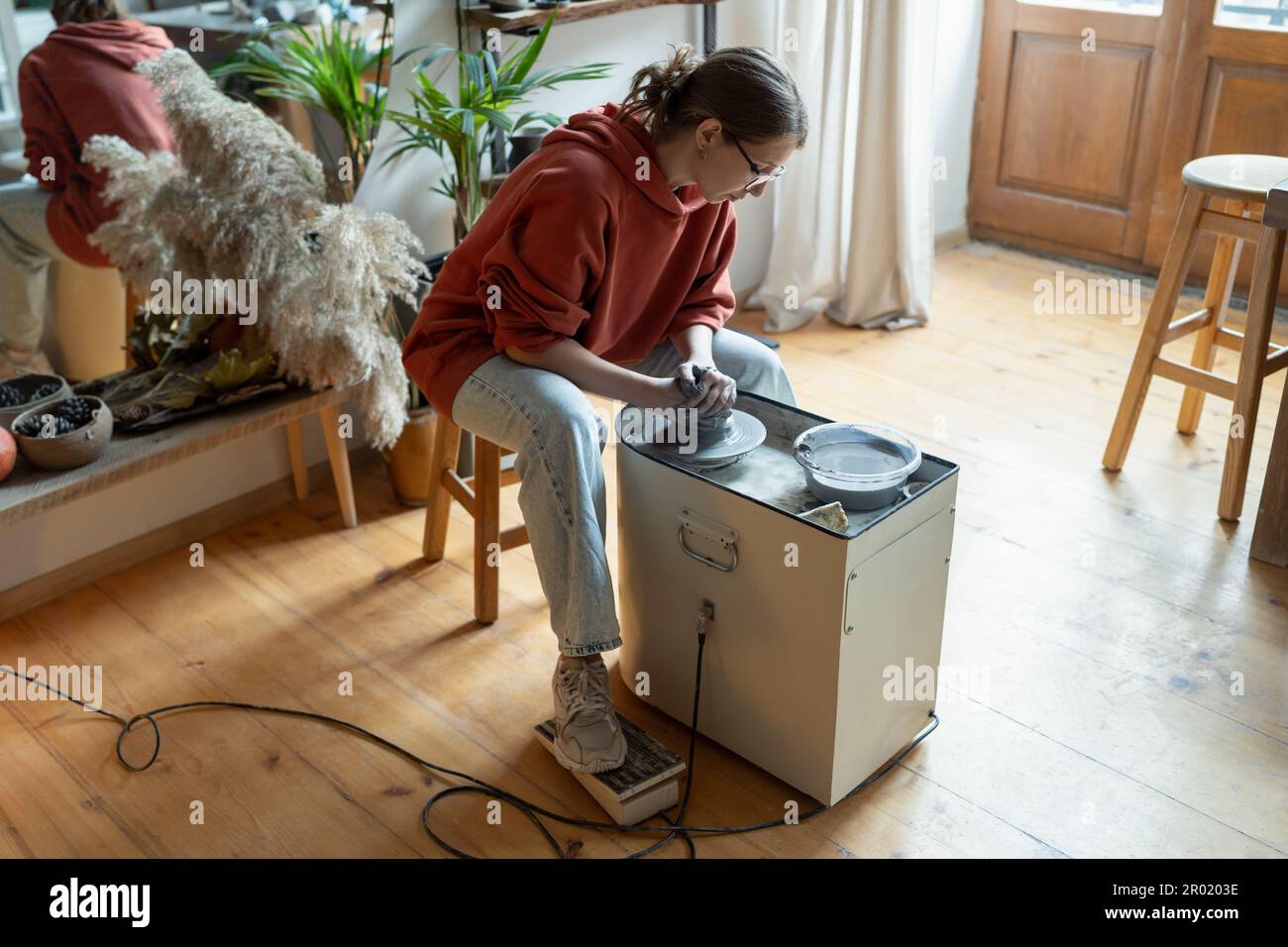 Concentrated craftswoman artist ceramist using potter wheel sits in ...