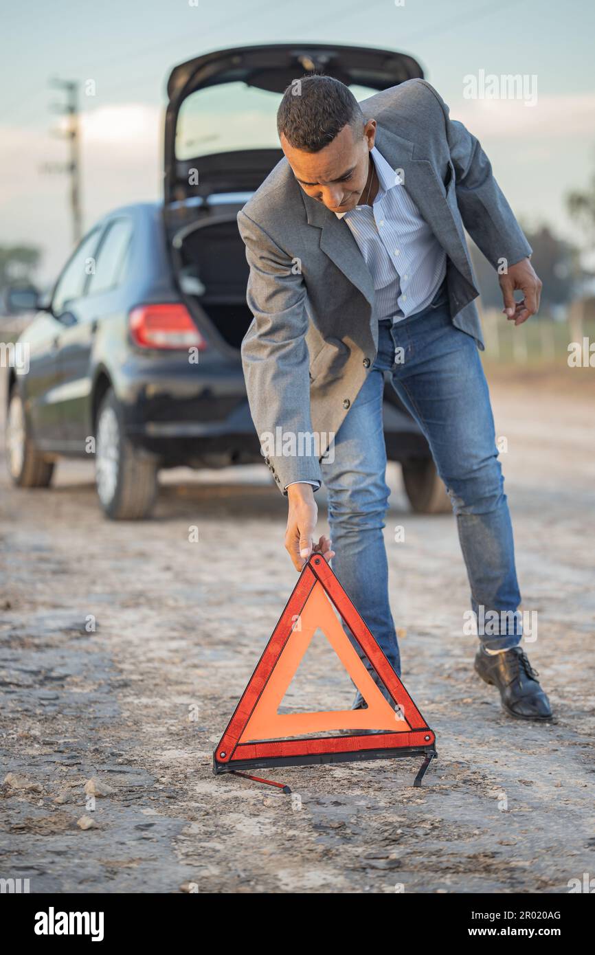Young Latino man placing a warning triangle behind a broken down car ...