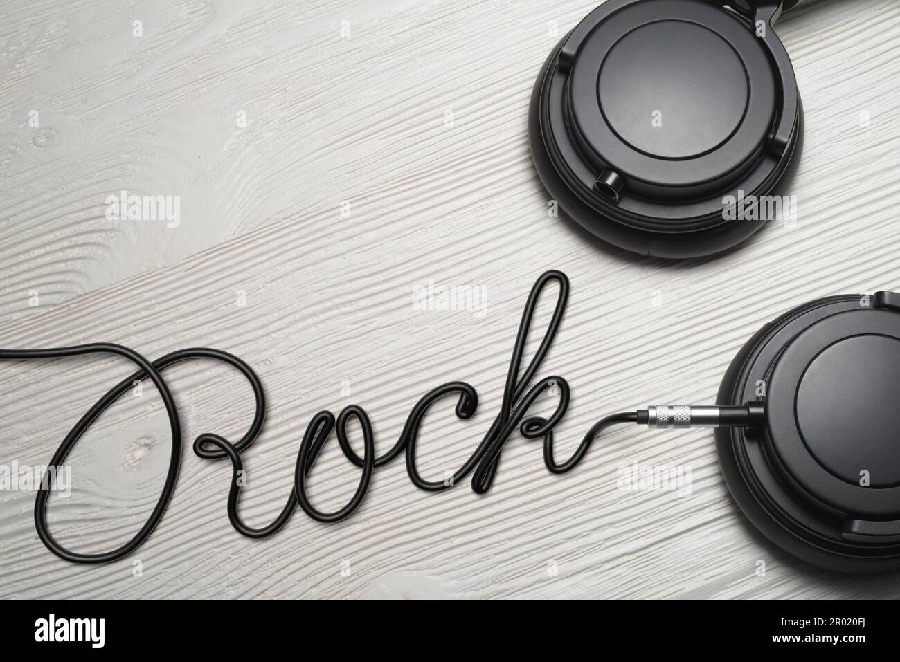 Headphones with Rock word shaped wire on the white wooden table. Music ...