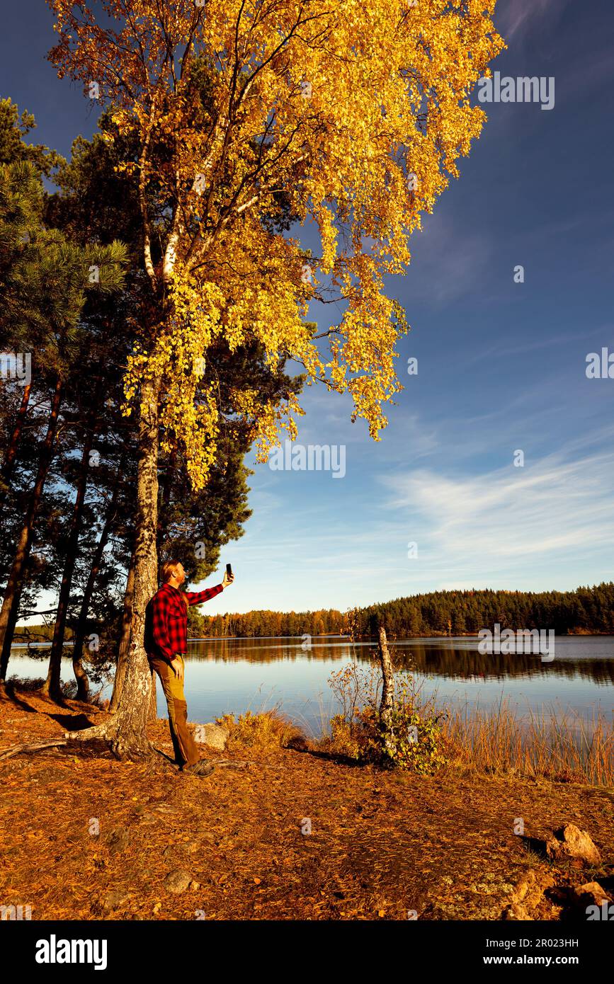 man standing against tree in fall foliage taking a self i with his ...