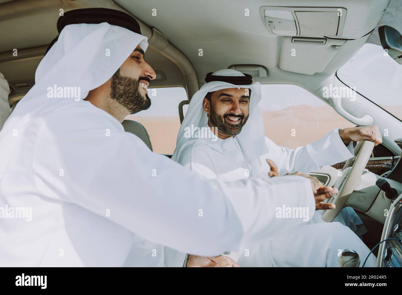 Two middle-eastern men wearing traditional emirati arab kandura driving a 4x4 car in the desert ...
