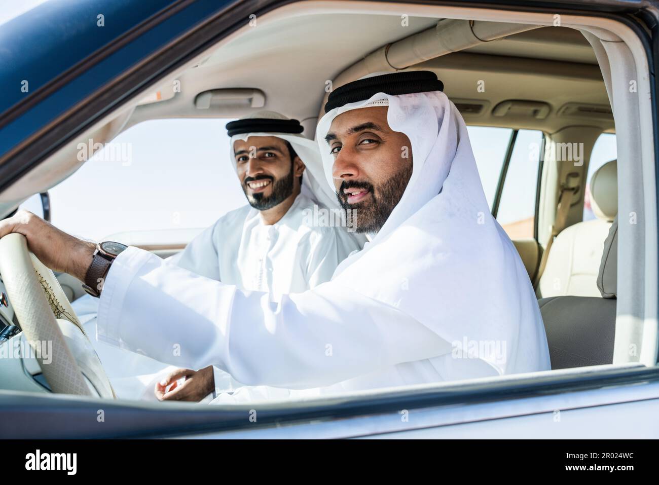 Two middle-eastern men wearing traditional emirati arab kandura driving ...