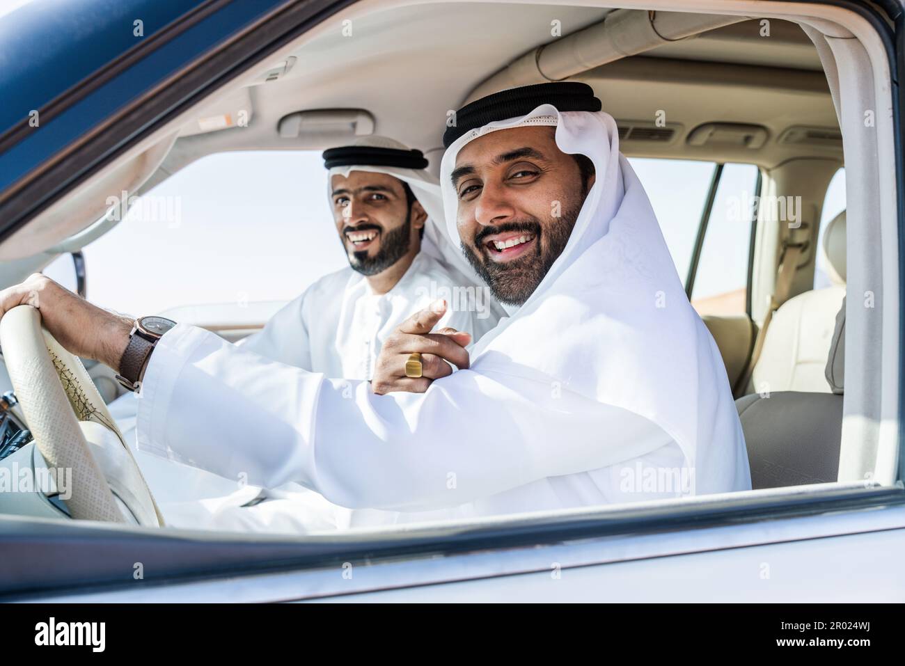 Two middle-eastern men wearing traditional emirati arab kandura driving ...