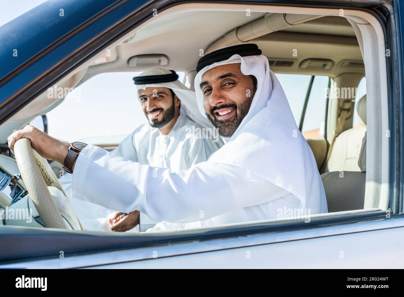 Two middle-eastern men wearing traditional emirati arab kandura driving ...