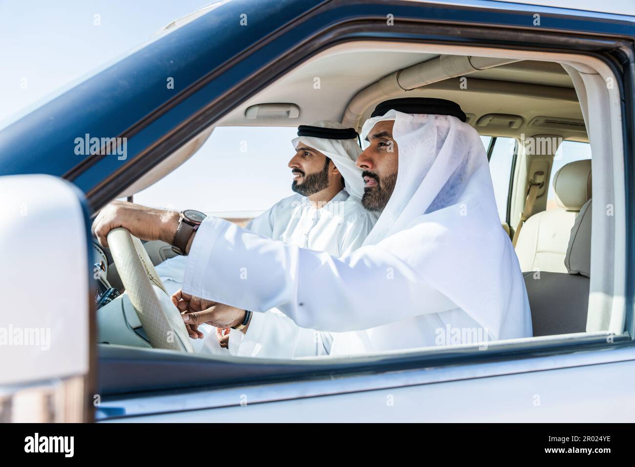 Two middle-eastern men wearing traditional emirati arab kandura driving a 4x4 car in the desert ...