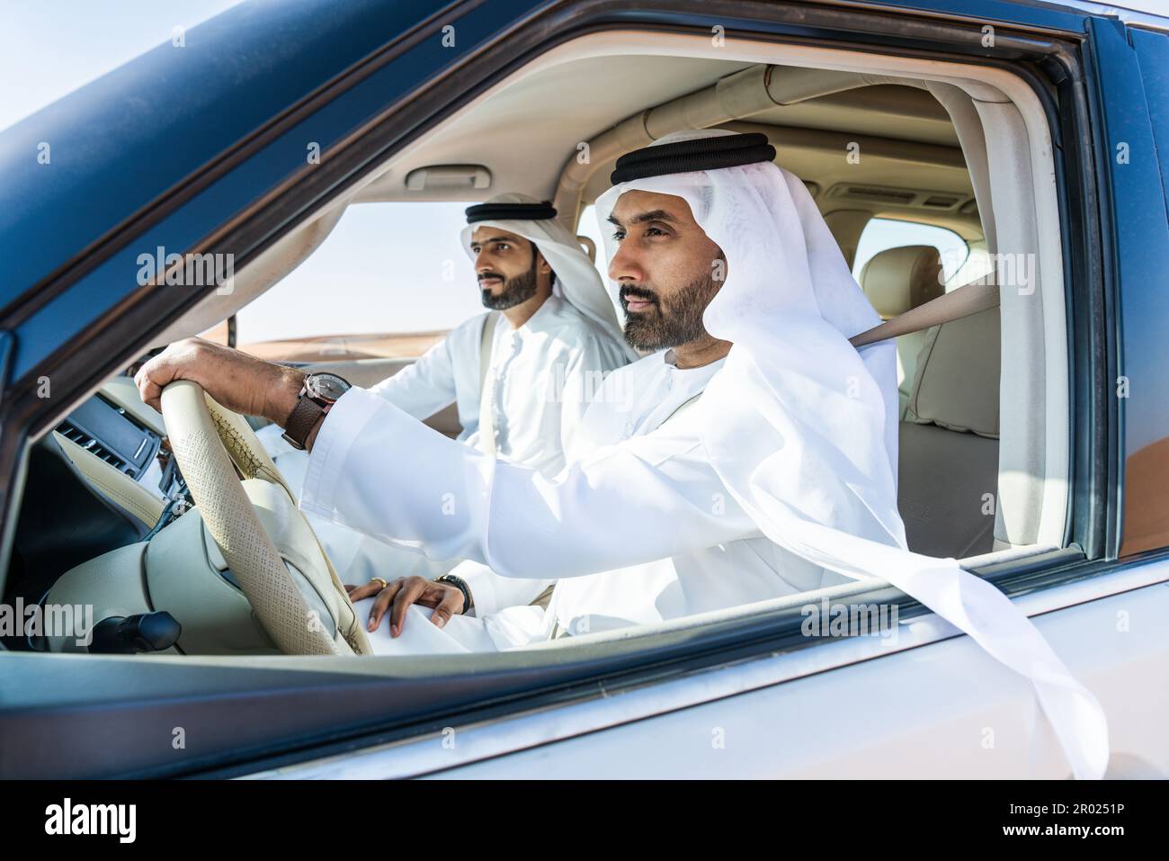 Two middle-eastern men wearing traditional emirati arab kandura driving ...