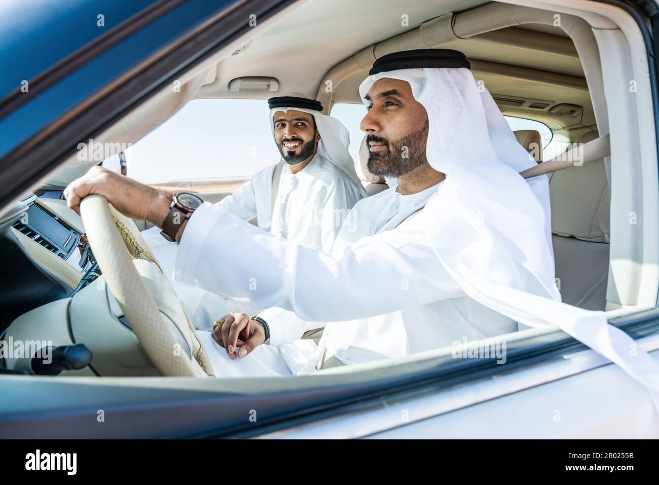 Two middle-eastern men wearing traditional emirati arab kandura driving ...