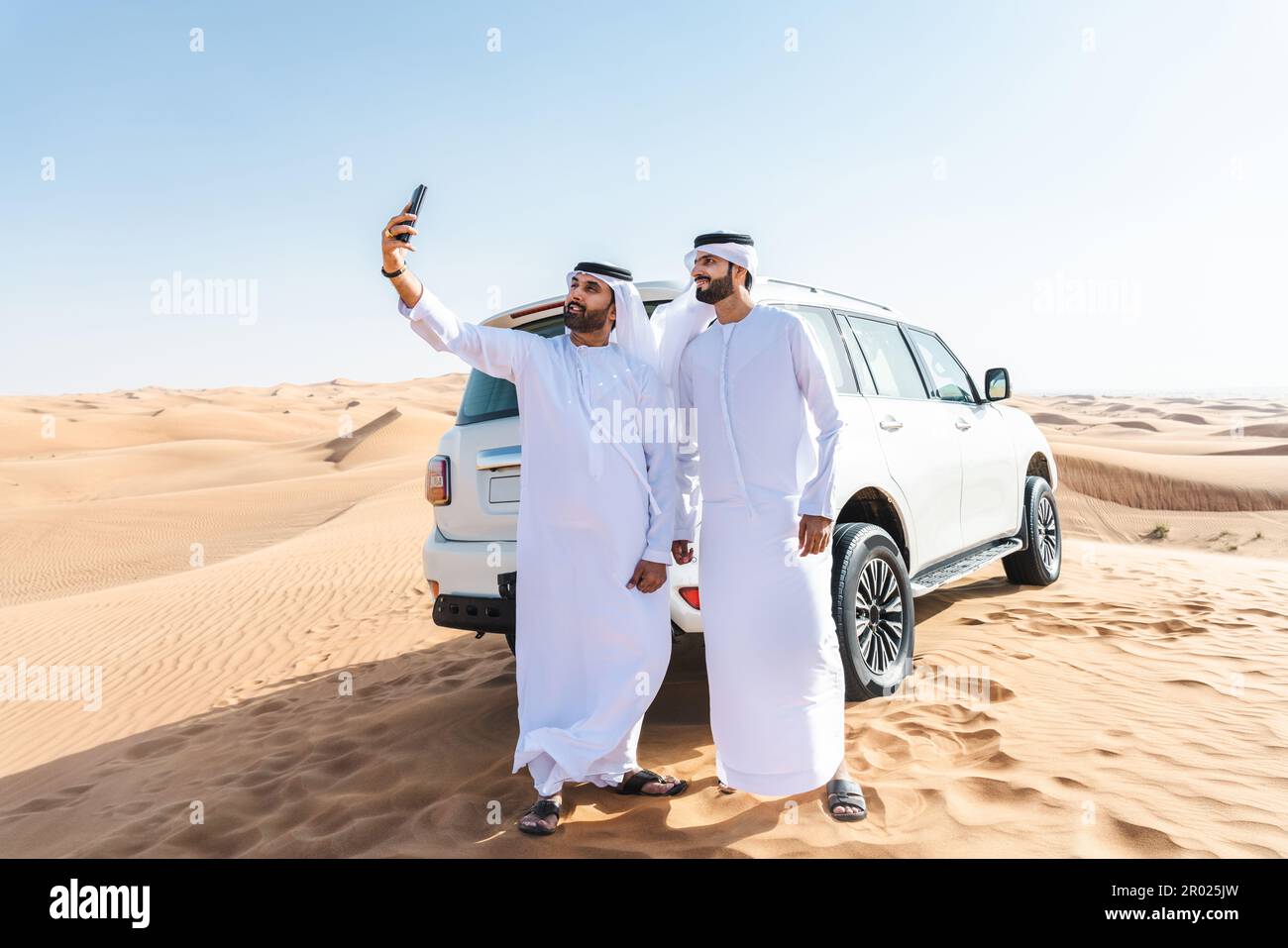 Two middle-eastern men wearing traditional emirati arab kandura driving ...