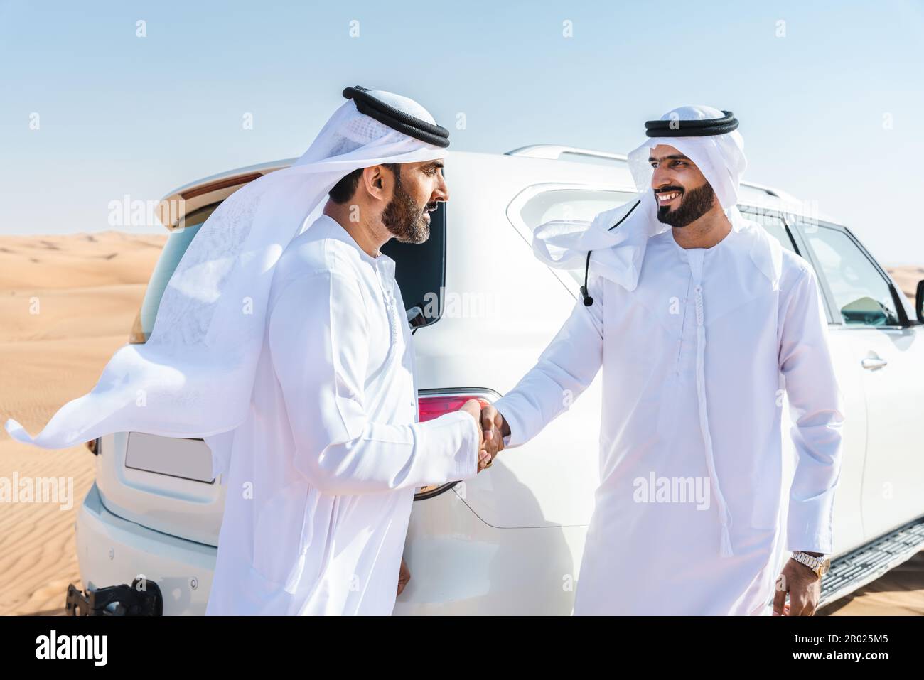 Two middle-eastern men wearing traditional emirati arab kandura driving ...