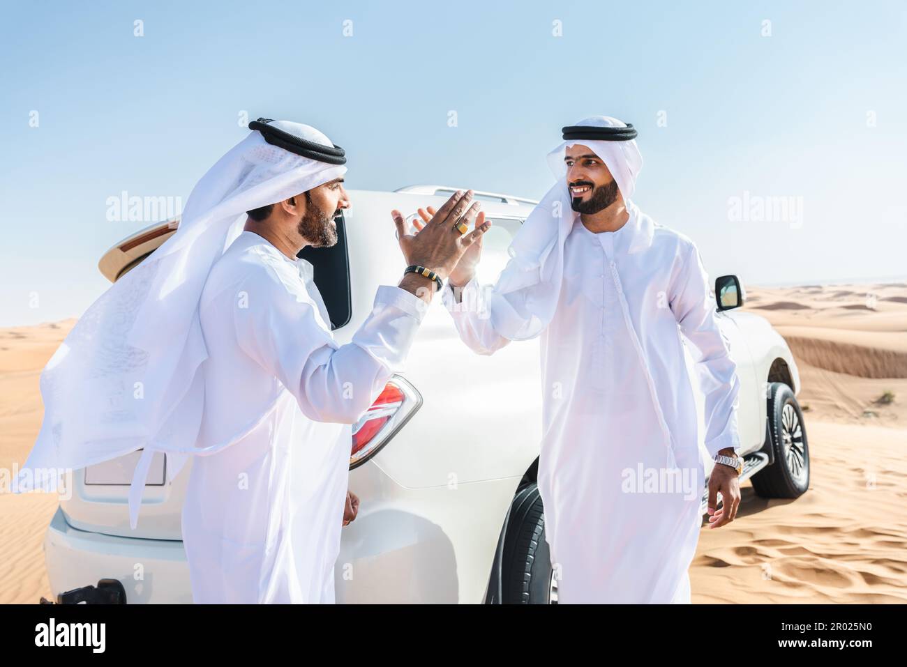 Two middle-eastern men wearing traditional emirati arab kandura driving ...